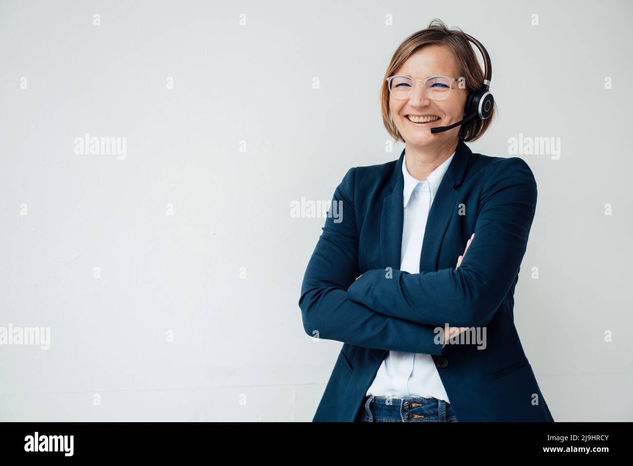 Happy telecaller wearing headset standing with arms crossed against ...