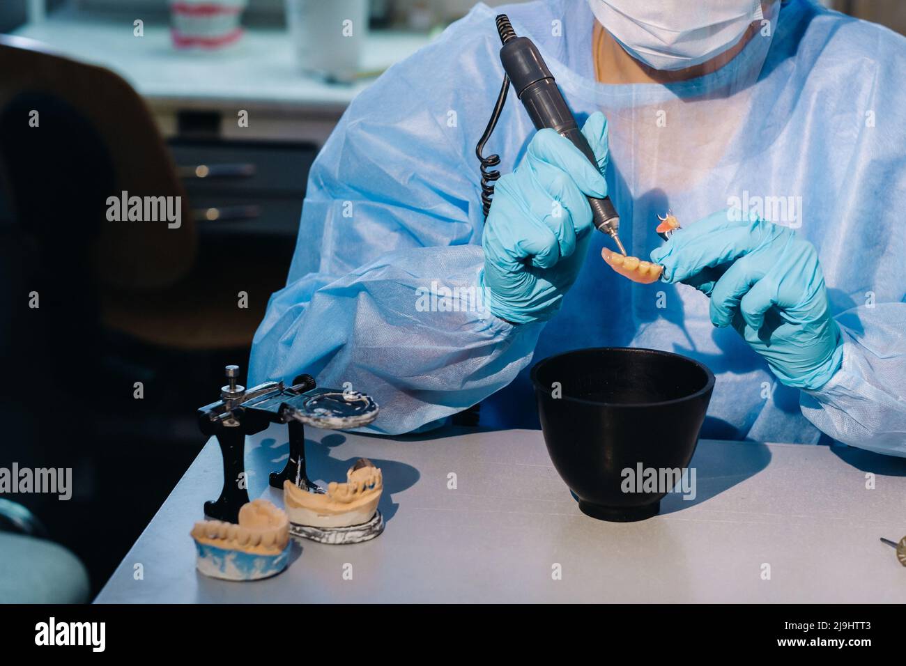 A masked and gloved dental technician works on a prosthetic tooth in ...