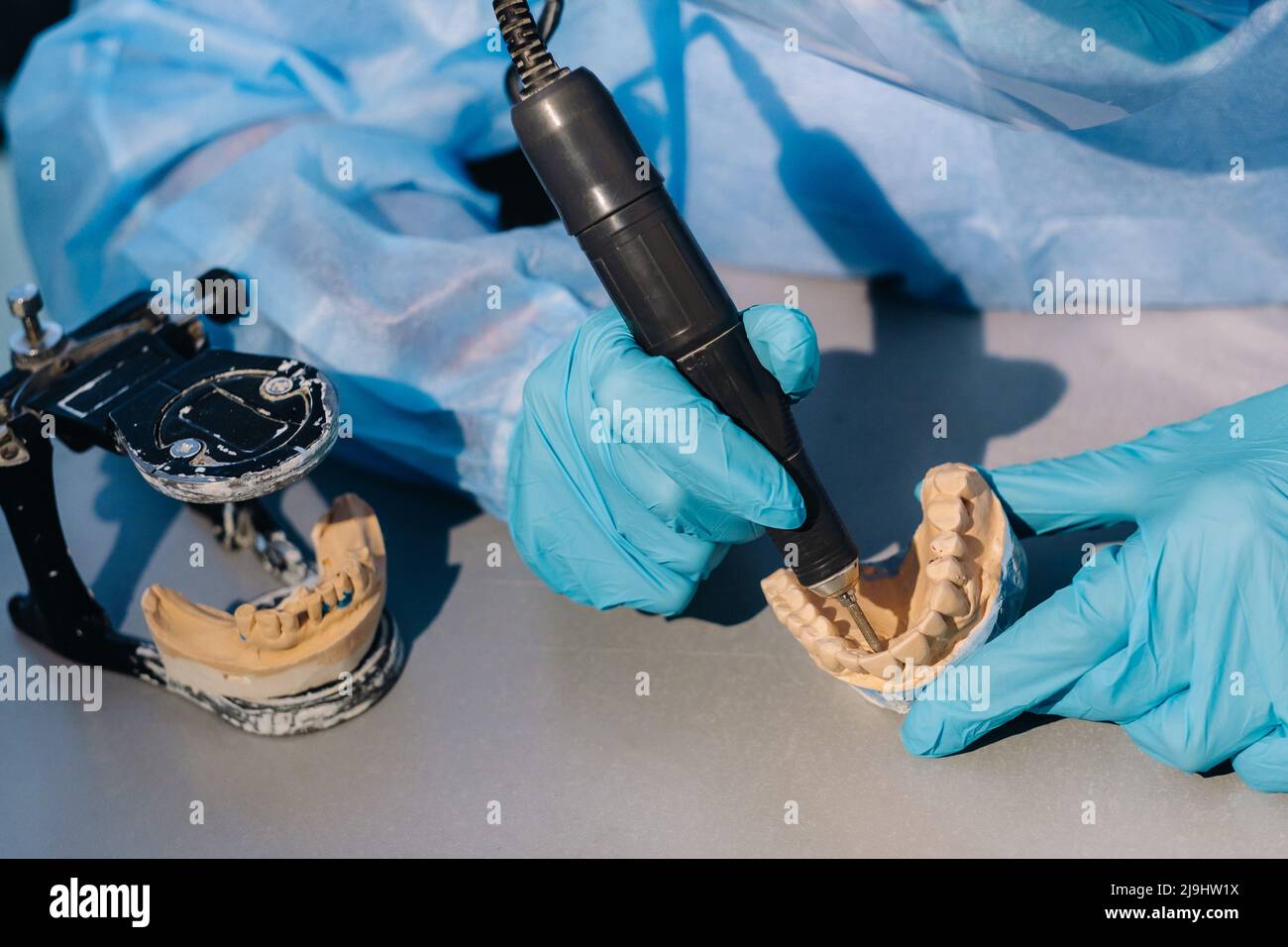 A masked and gloved dental technician works on a prosthetic tooth in ...
