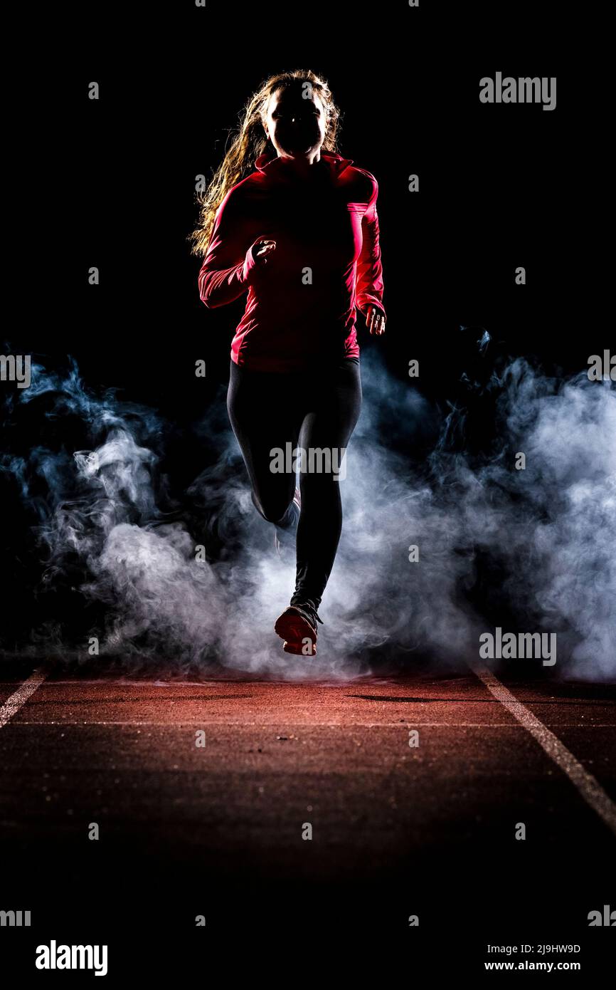 Young woman jogging on running track amidst fog in dark at night Stock ...