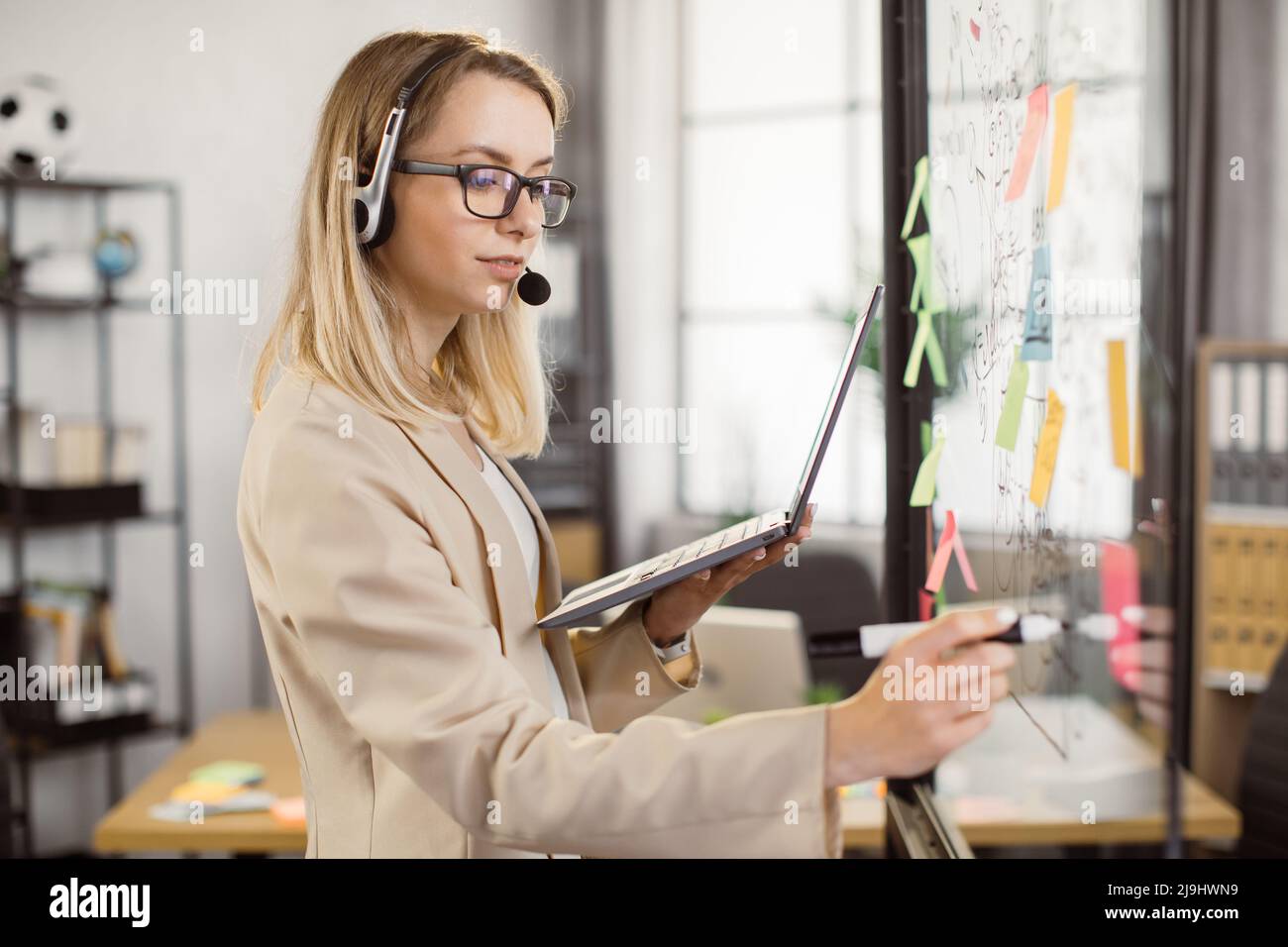 Female office manager in headset making notes on glass board during ...