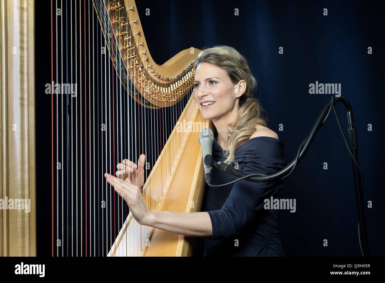 Smiling mature woman playing harp in front of black background Stock ...