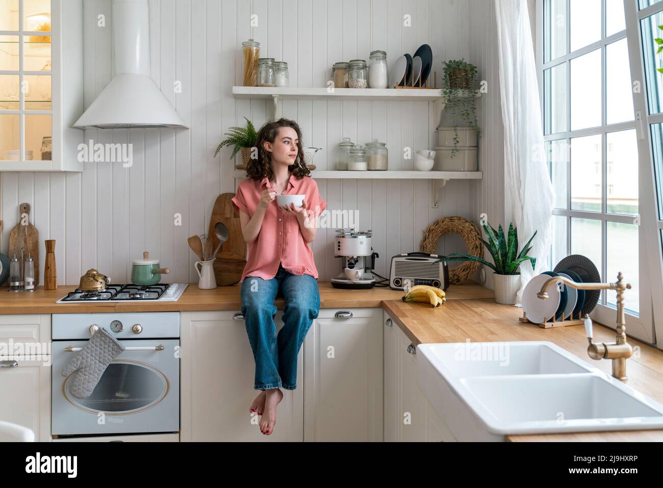 Woman with bowl sitting on kitchen counter at home Stock Photo - Alamy
