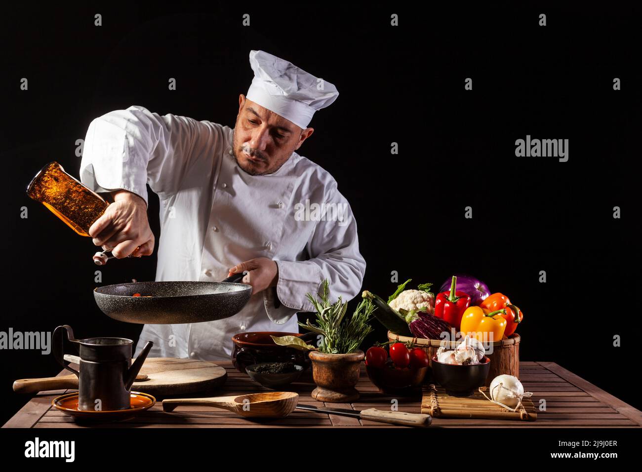 Male chef in white uniform pouring vinegar onto the cooking pan with ...