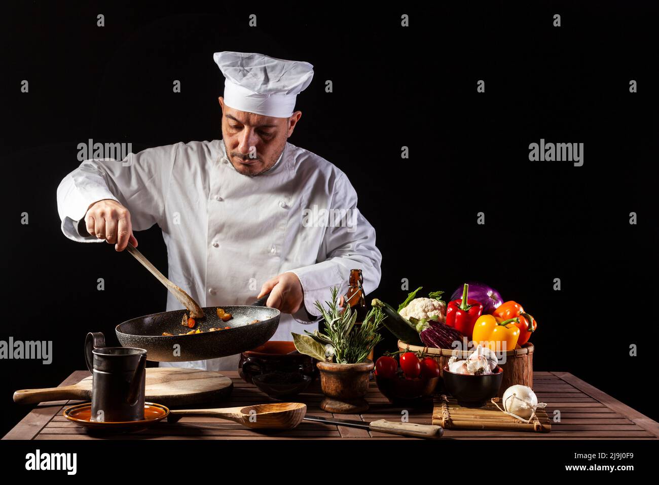 Male cook in white uniform and hat with ladle mixes the ingredients ...
