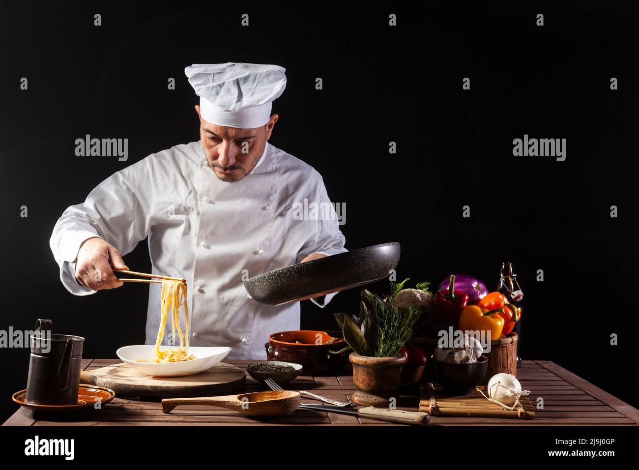 Male chef in white uniform prepares spaghetti with vegetables on the ...