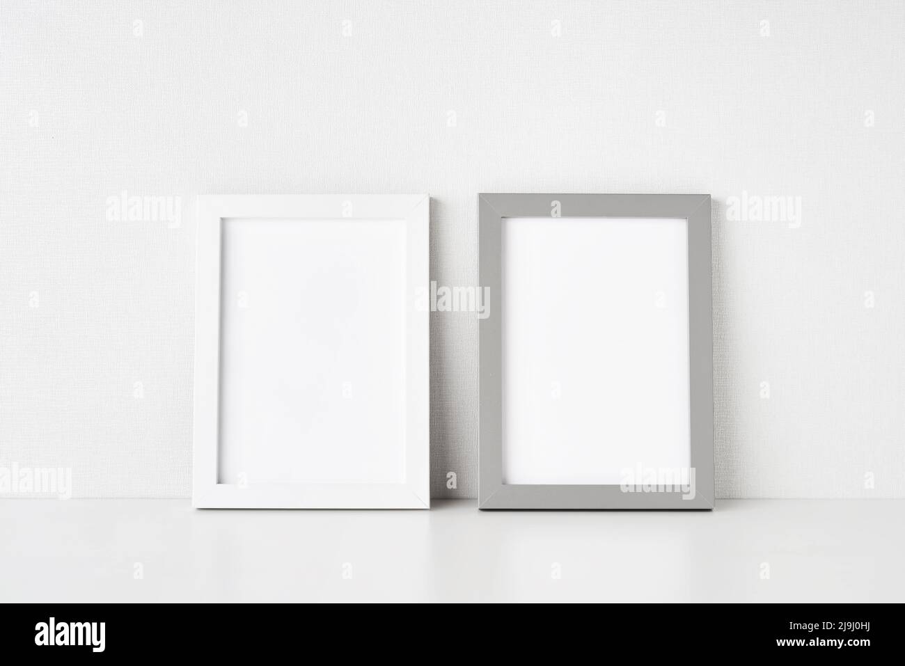 Two empty picture frames are placed on the white table by the wall ...