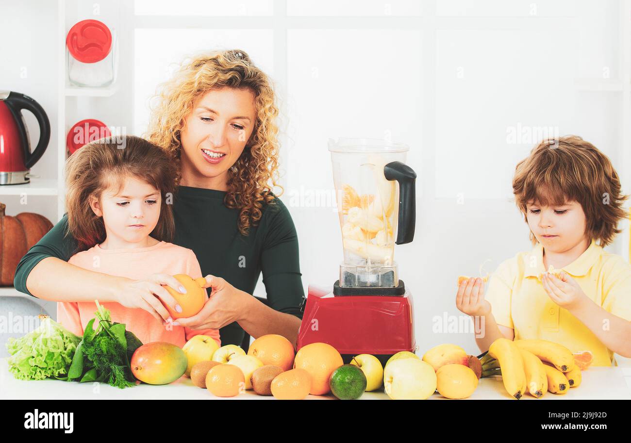 Mother with children making smoothie in a white kitchen. Family mother ...