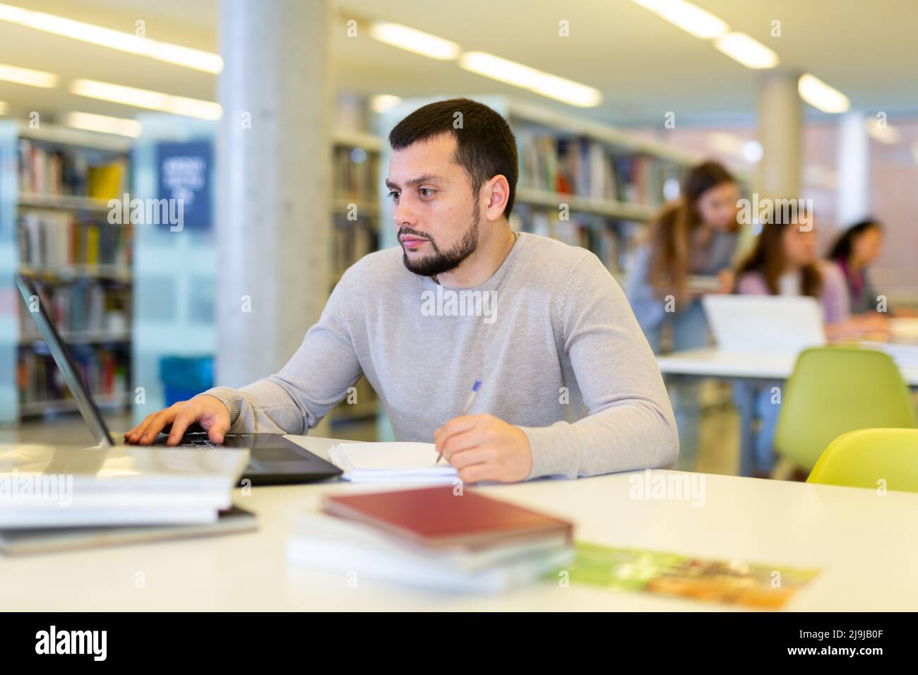 Focused young student studying with books and laptop in library Stock ...