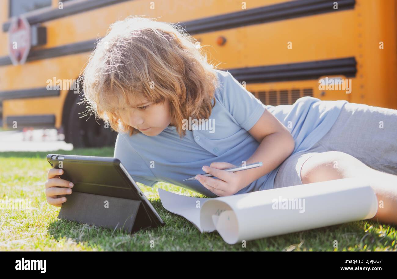 Child does school homework laying on grass in the park near school bus ...