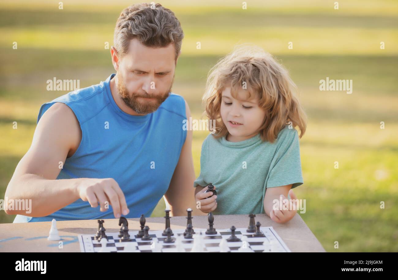Son laying on grass and playing chess with father. Concentrated kid boy ...