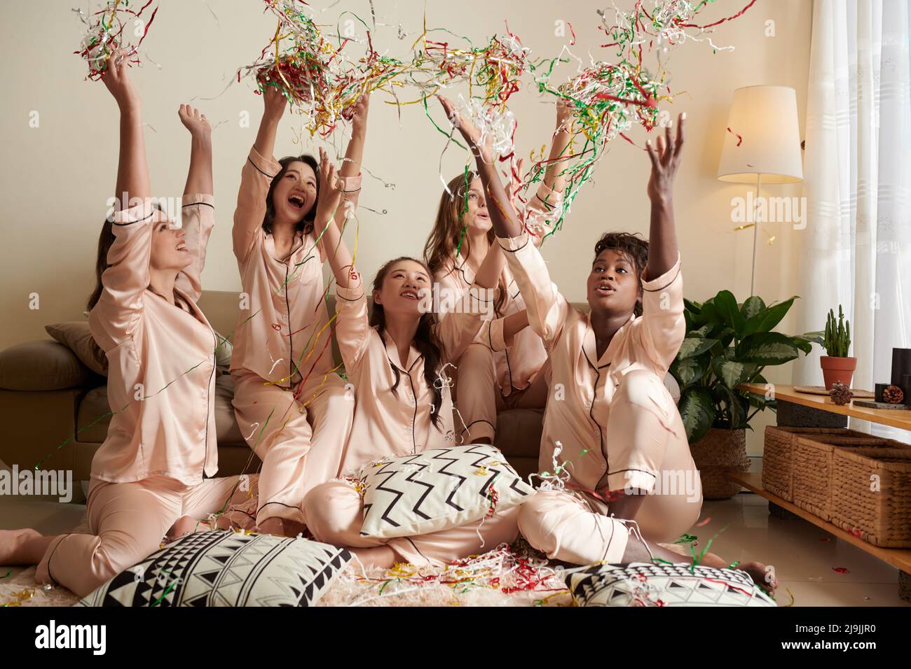Group pf excited young women in satin pajamas throwing holographic ...