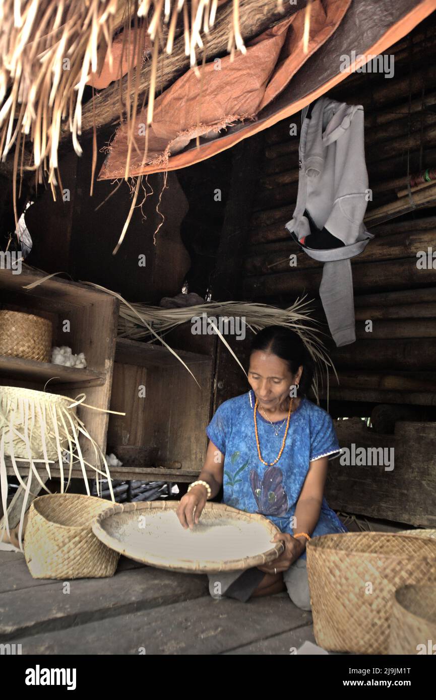 A senior woman cleaning rice before cooking at the porch of a house in ...