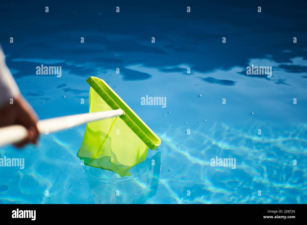 Man with skimmer net equipment cleaning swimming pool from rubbish ...