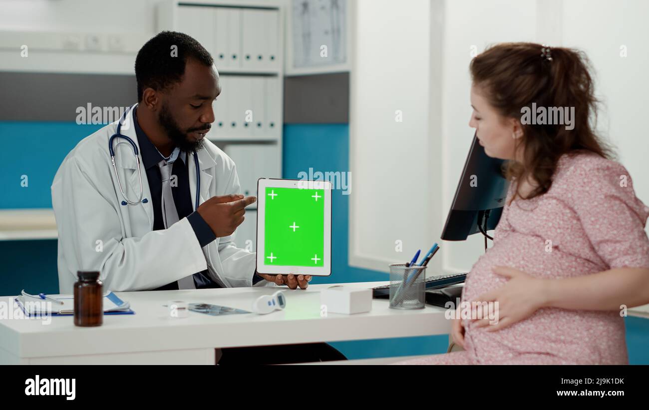 Pregnant woman and specialist looking at greenscreen on digital tablet ...