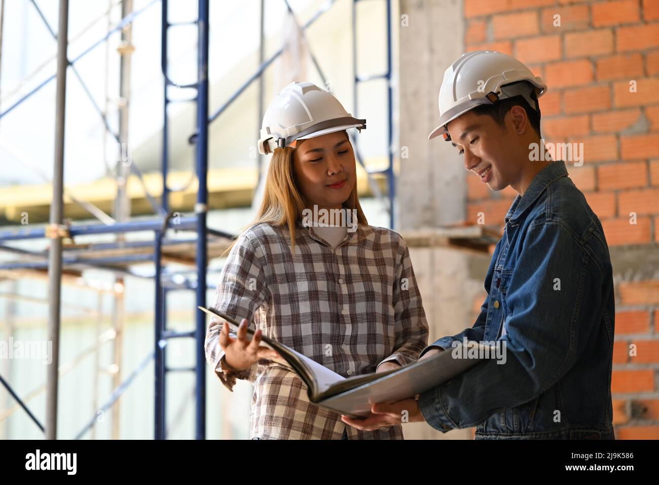Two architects wearing safety helmet working on blueprints at ...