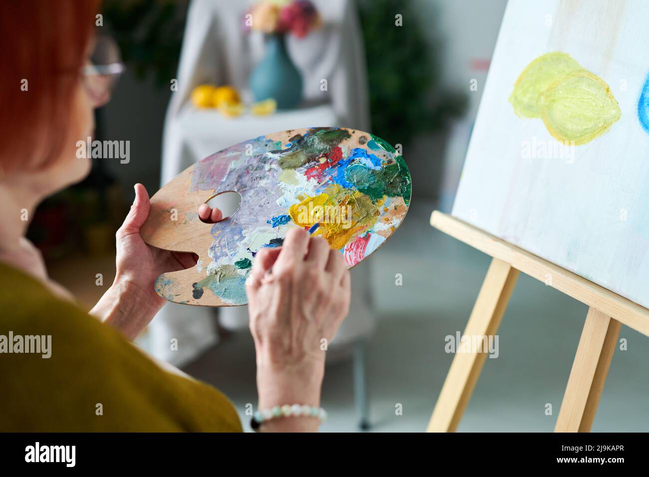 Close-up of woman mixing paints with paintbrush on palette and painting ...