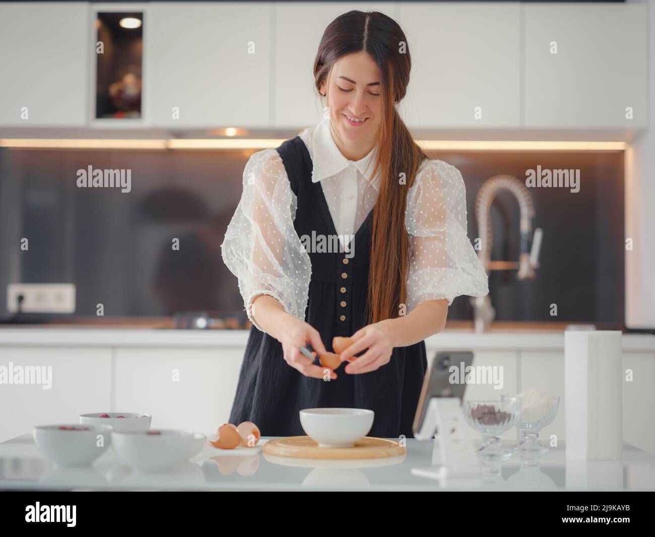 Beautiful young woman smiling while baking in kitchen at home ...