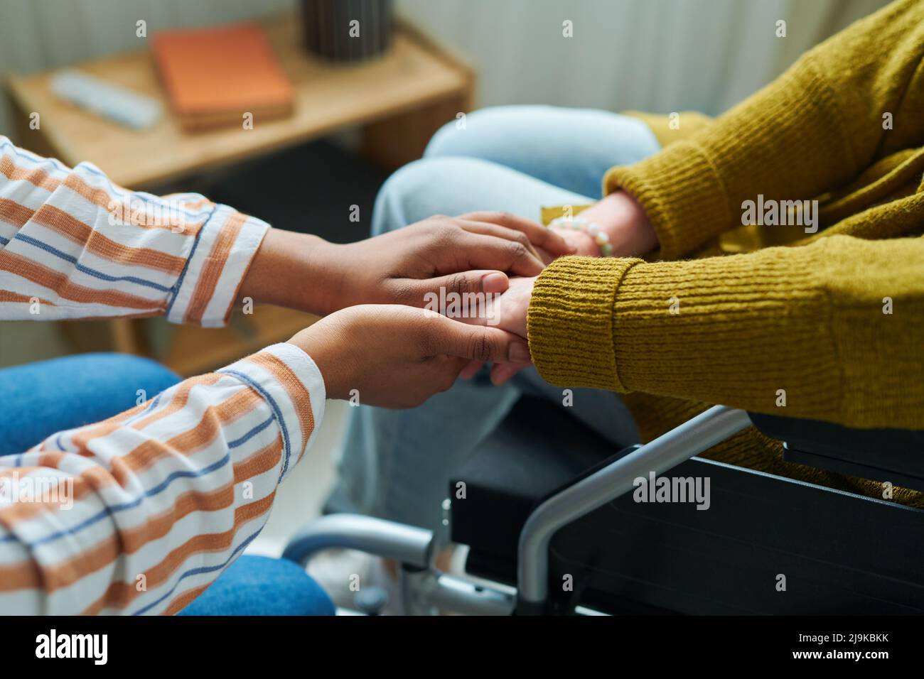 Close-up of caregiver holding hands with senior woman in wheelchair ...