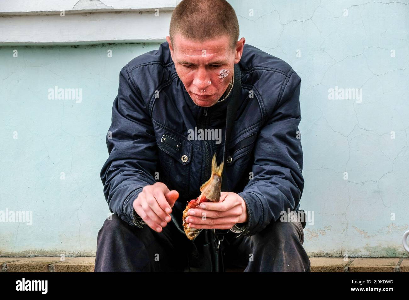 A man seen eating dry fish in front of the house of culture. Lysychansk ...