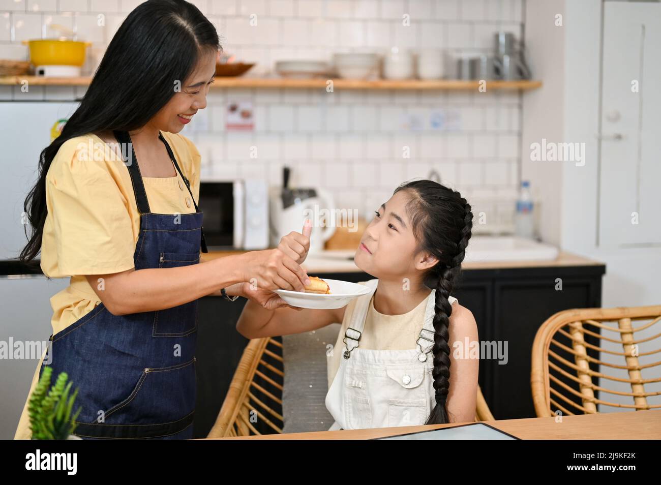Asian young mother is giving her daughter fresh baked cookies to taste ...