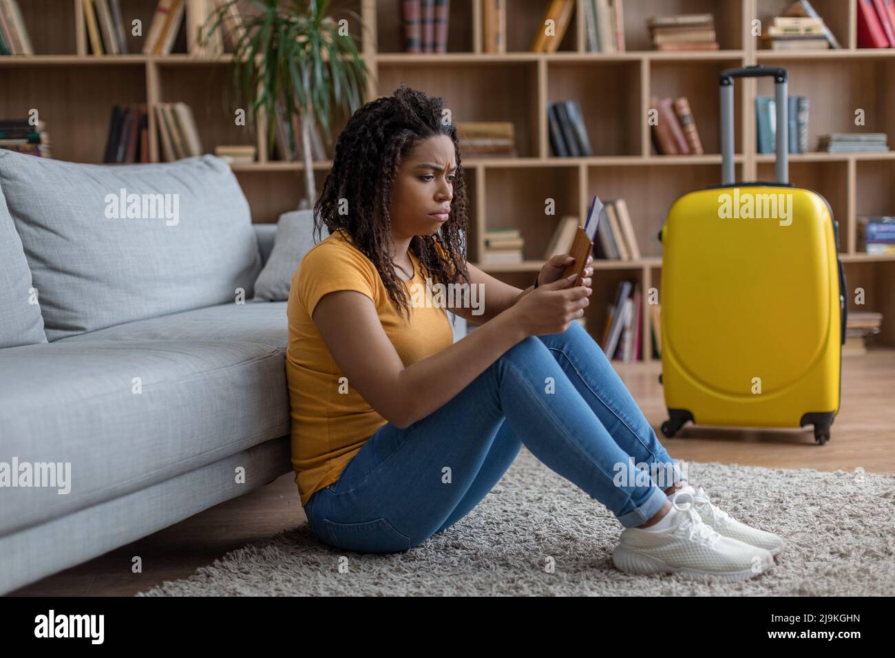 Unhappy black female tourist sitting on floor near suitcase and holding ...