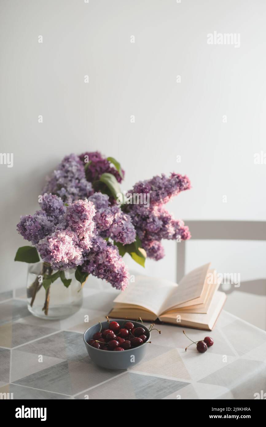 Romantic still life with an open book, lilac flowers and cherries on a ...
