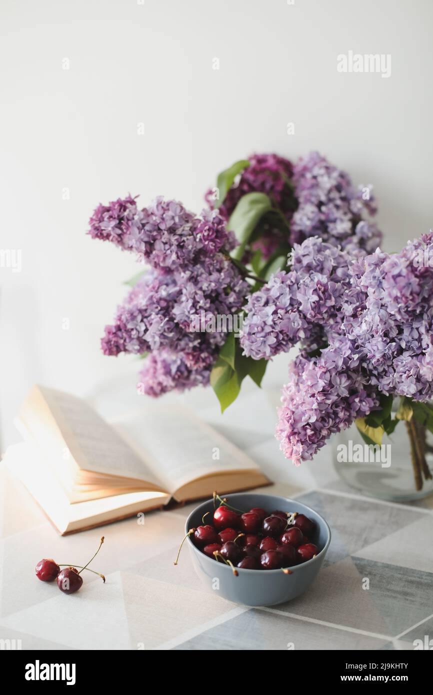 Romantic still life with an open book, lilac flowers and cherries on a ...