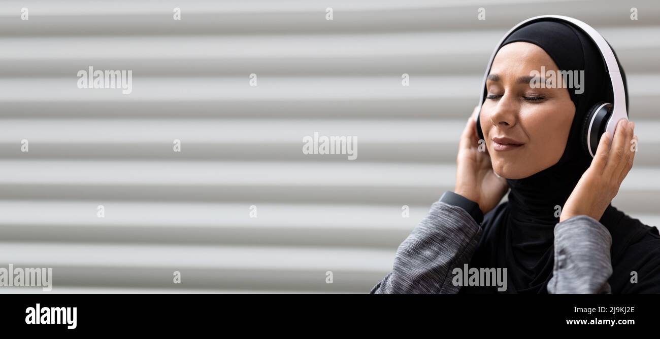 Satisfied young islamic lady in hijab in wireless headphones enjoy ...