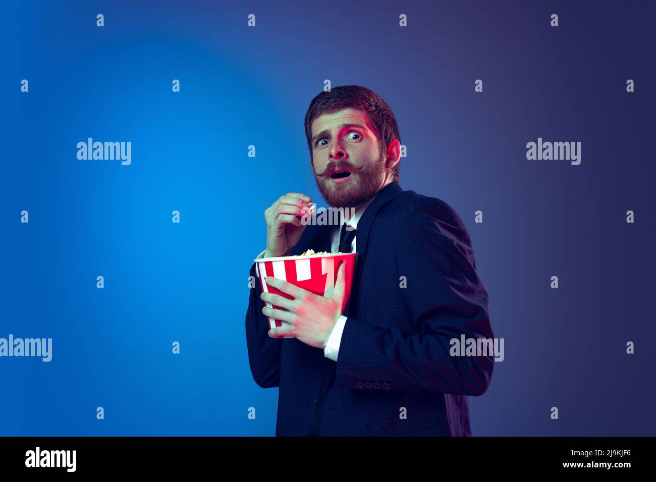 Young scared man in business suit eating popcorn and watching movie ...