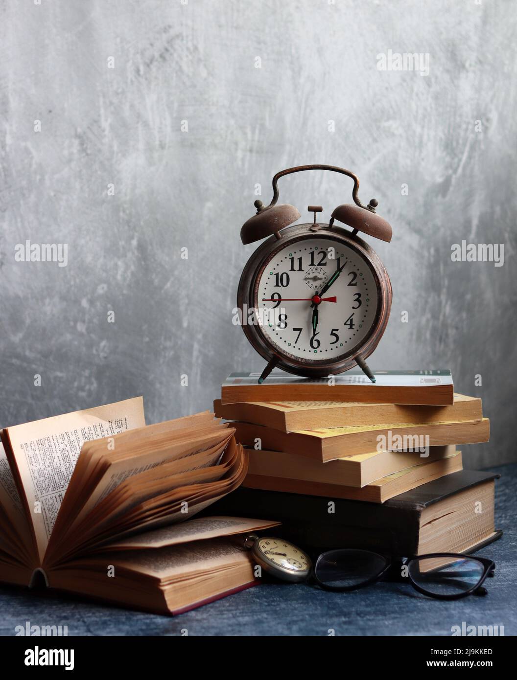 Stack of old books, vintage watch on a desk. Light grey textured ...