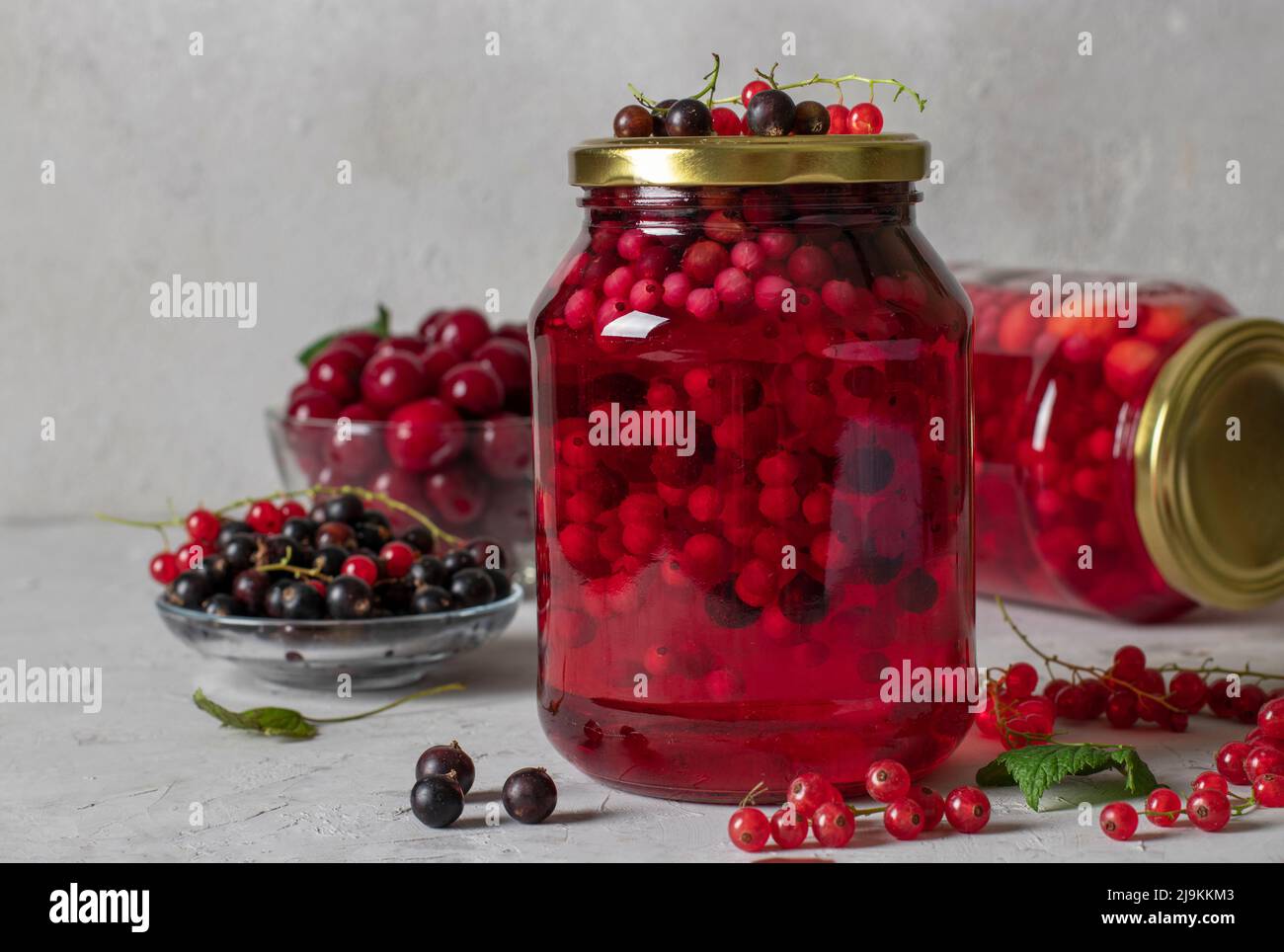 Homemade canned compote with cherries and currants in two jars on light ...