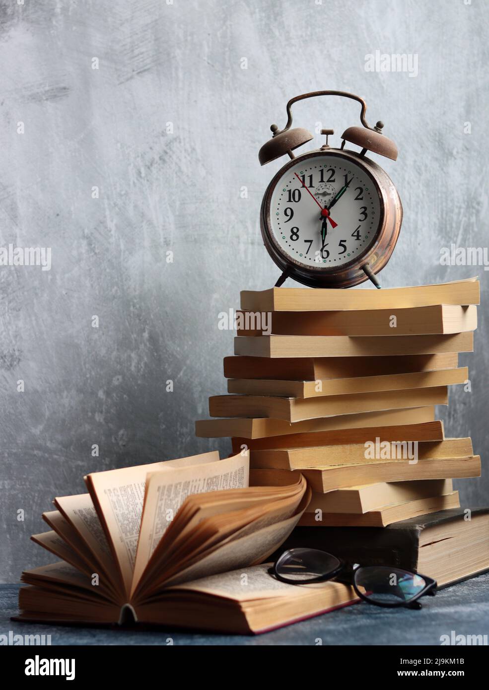 Stack of old books, vintage watch on a desk. Light grey textured ...