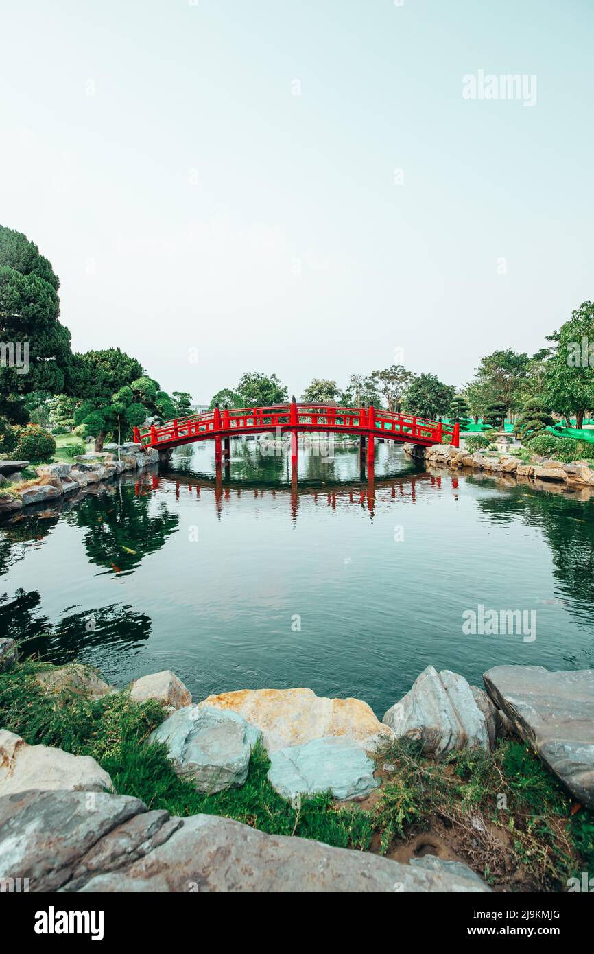 Red bridge in a Japanese garden park with a lake surrounded by rocks as ...