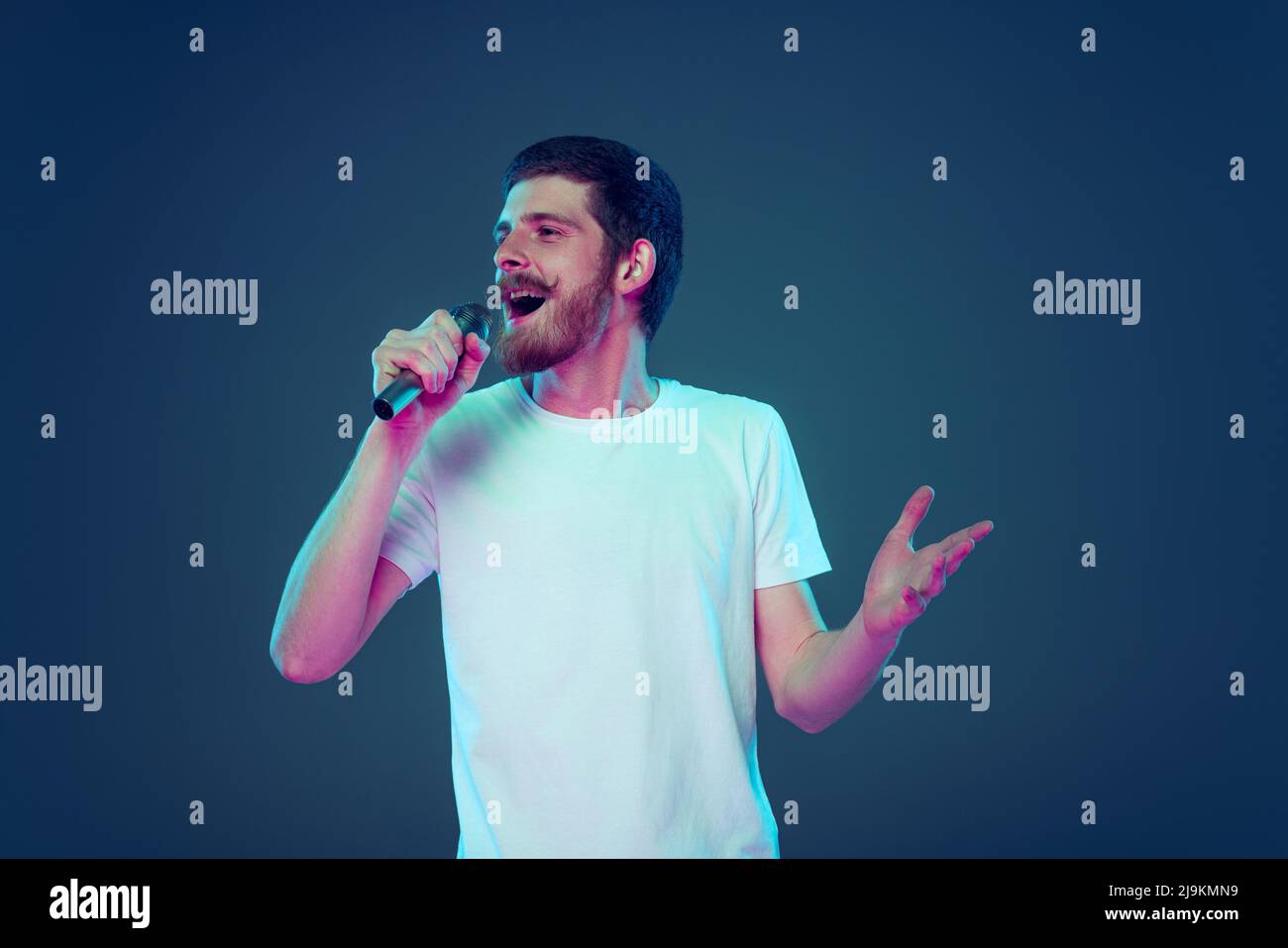 Handsome man in white t-shirt singing at microphone isolated on dark ...