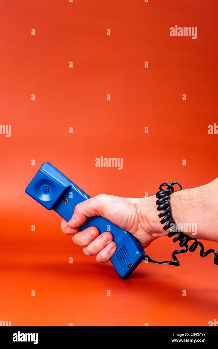 Hand holding a blue phone, with the phone cord wrapped around the arm ...