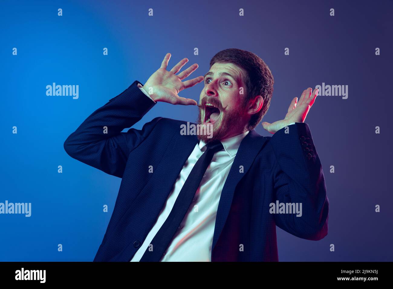 Excited young stylish man in business suit shouting isolated on dark ...