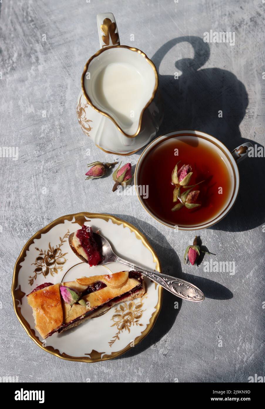 Still life with cup of tea, jug of milk, cherry pie, small rose flowers ...