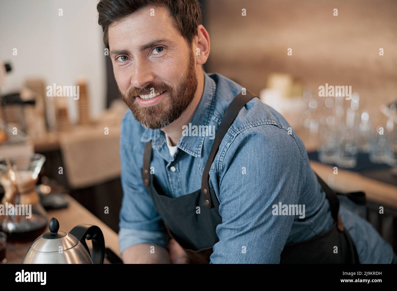 Barista with stylish beard smiling while behind a counter in the cafe ...