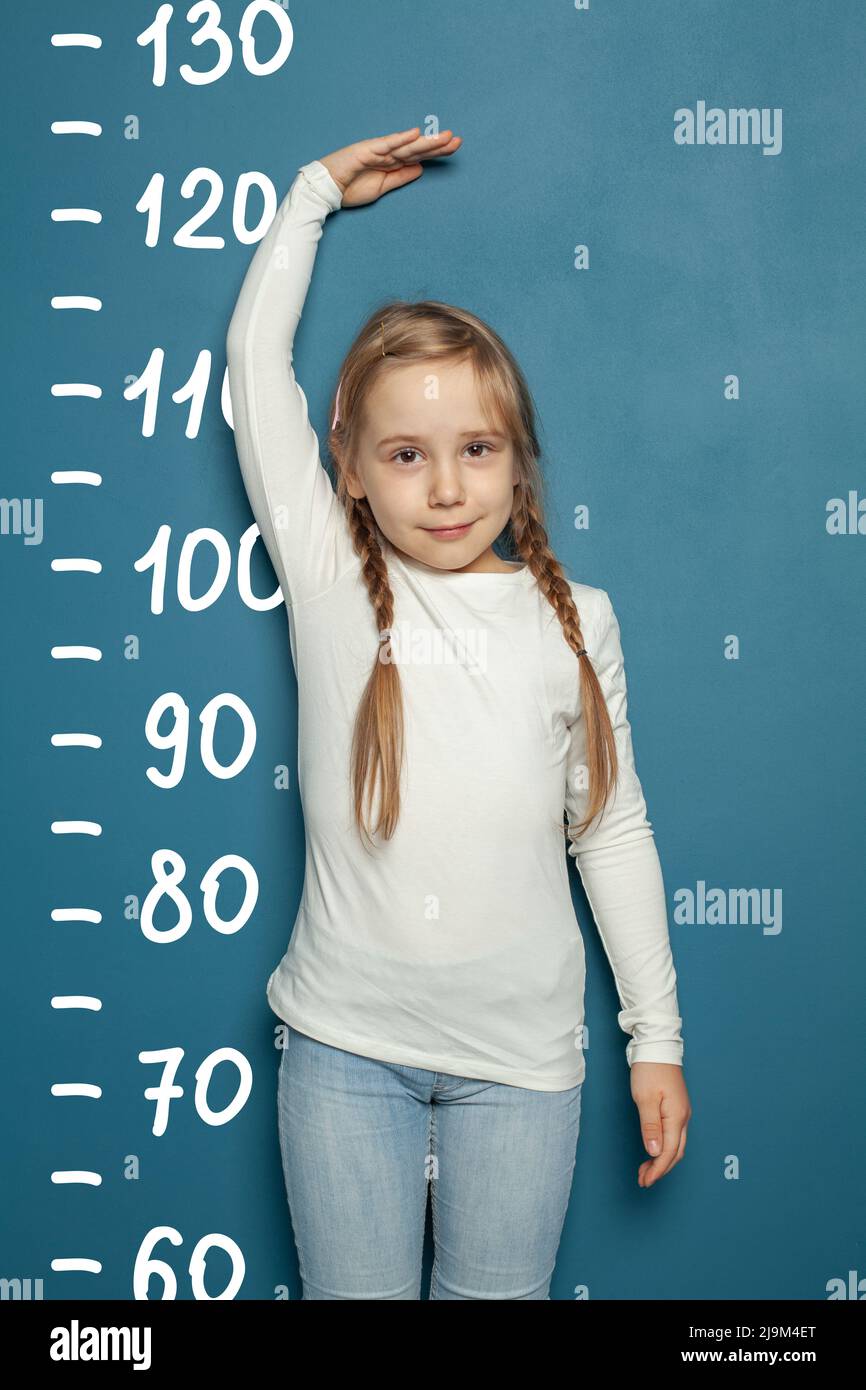 Cute little girl measuring height near blue wall background at home ...