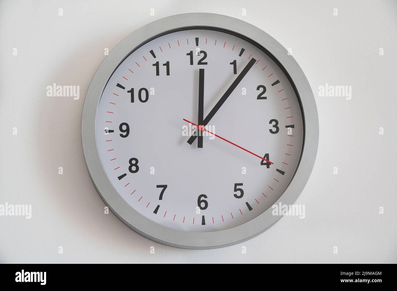 A modern analog wall clock showing time five minutes past twelve in a ...
