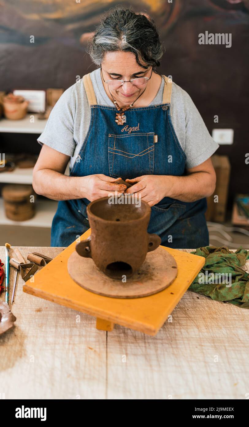 Happy mature focused female craftsWoman ceramist in apron shaping piece ...