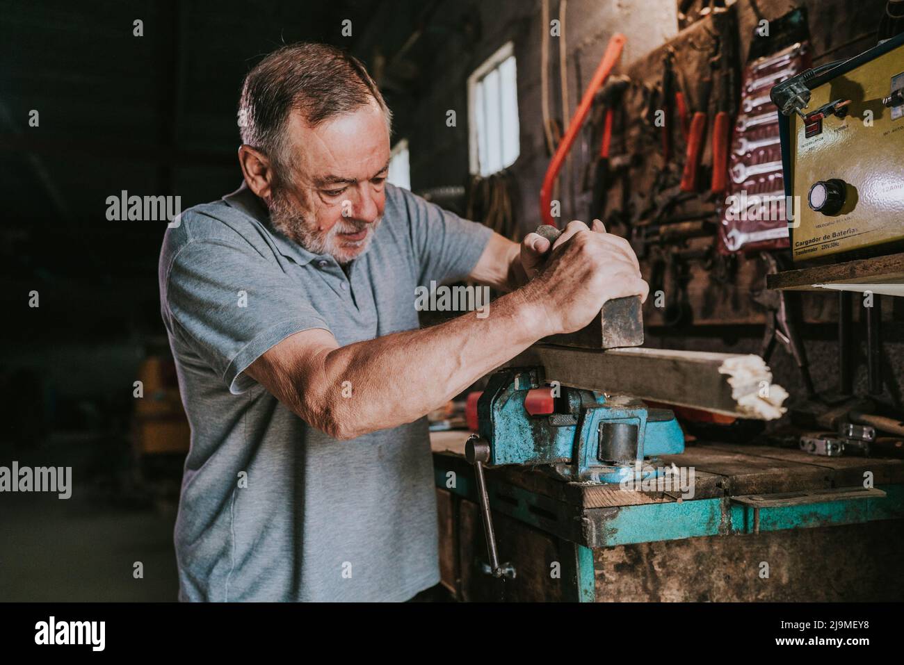 Focused mature male woodworker using jointer for planning wooden plank ...