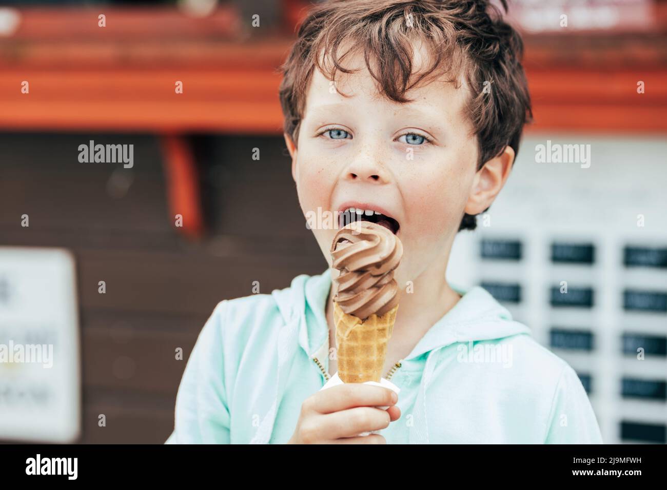 Cute boy with gray eyes looking at camera and licking sweet chocolate ...