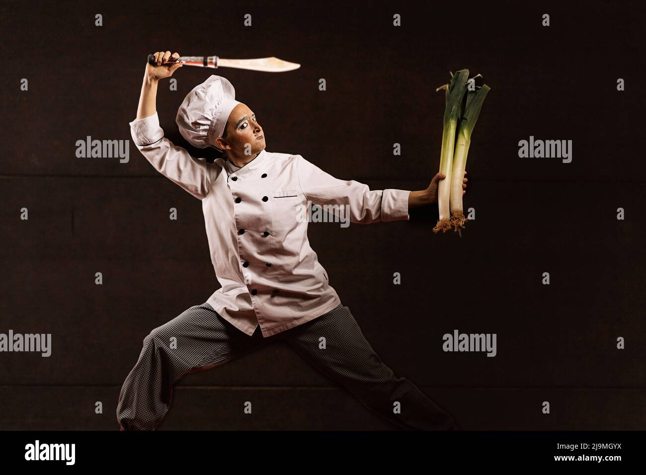 Funny young female clown in chef costume with makeup doing martial arts ...