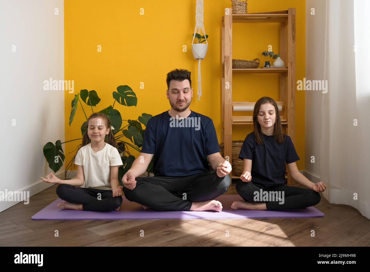 Relaxed dad and daughters in activewear sitting on mat in Padmasana ...