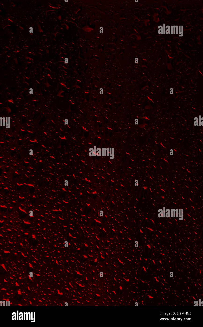 Raindrops on the window. Dark red toned black and white background ...