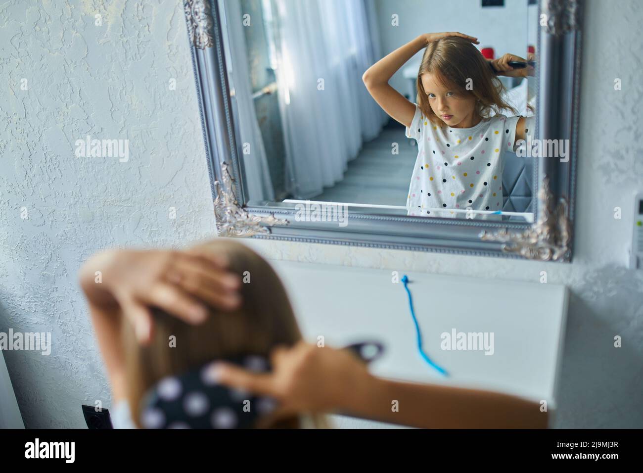 Pretty Little girl combing by herself hair in front of a mirror ...