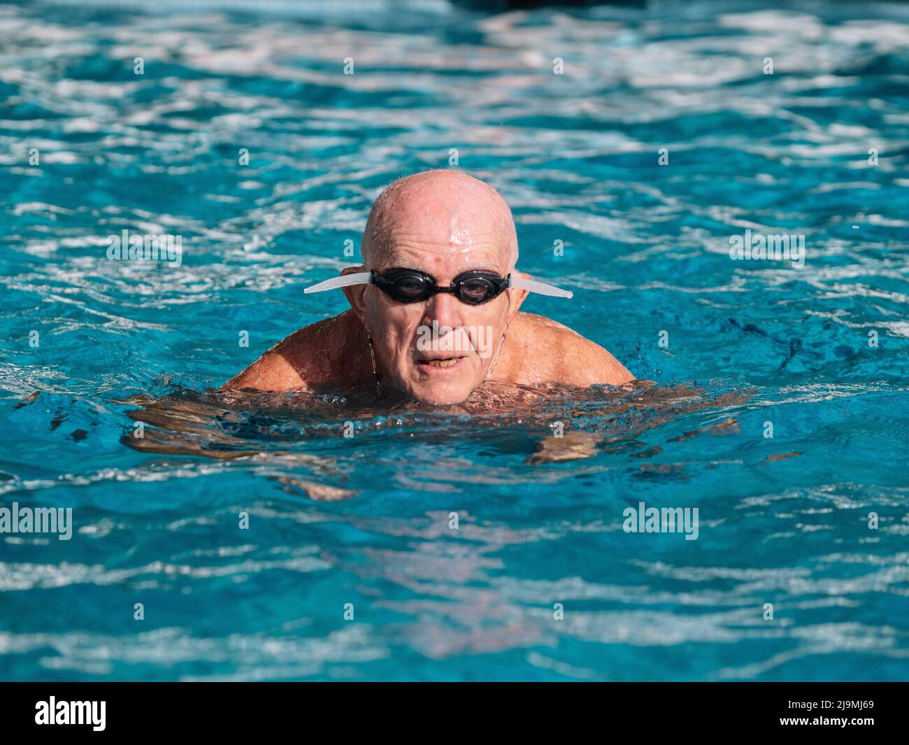 Bald elderly male in goggles swimming in rippling water of outdoor pool ...