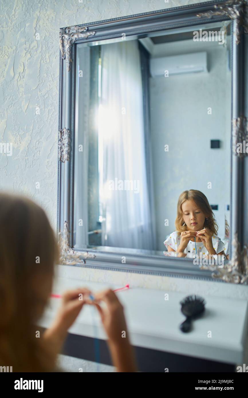 Pretty Little girl combing by herself hair in front of a mirror ...